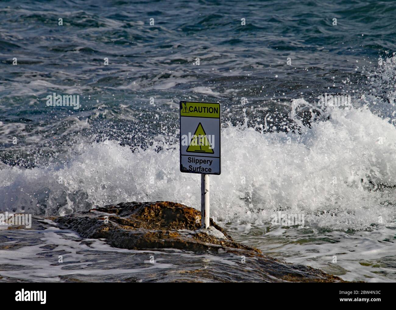 Sign on the rocks in the sea giving the obvious warning of slippery ...