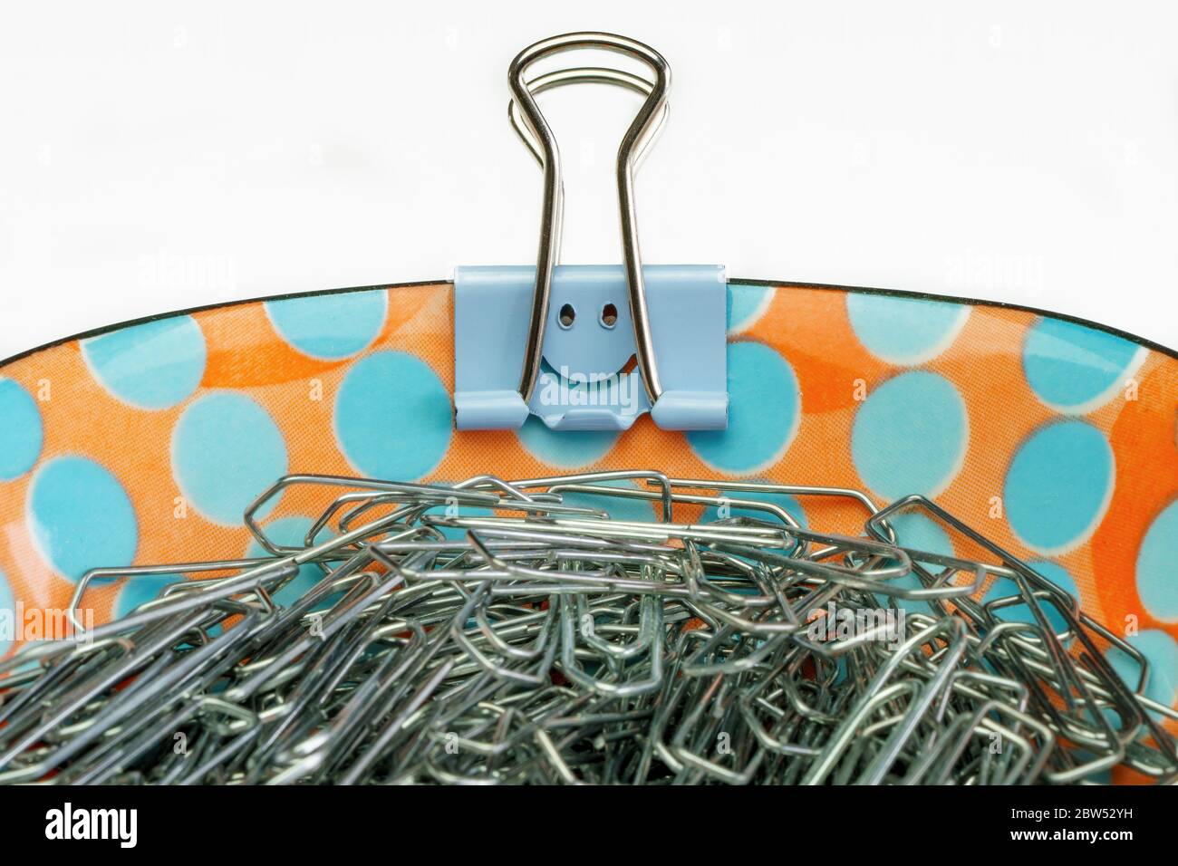 A porcelain bowl with paper clips and a blue smiley paper clip on the ...