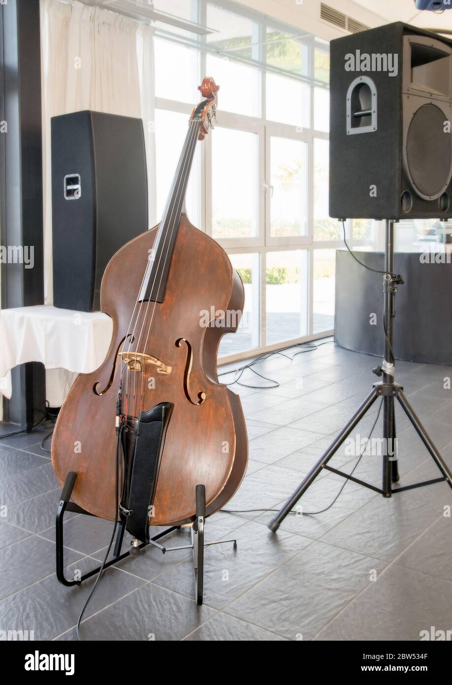 Old wooden double bass next to a speaker in an interior without people ...