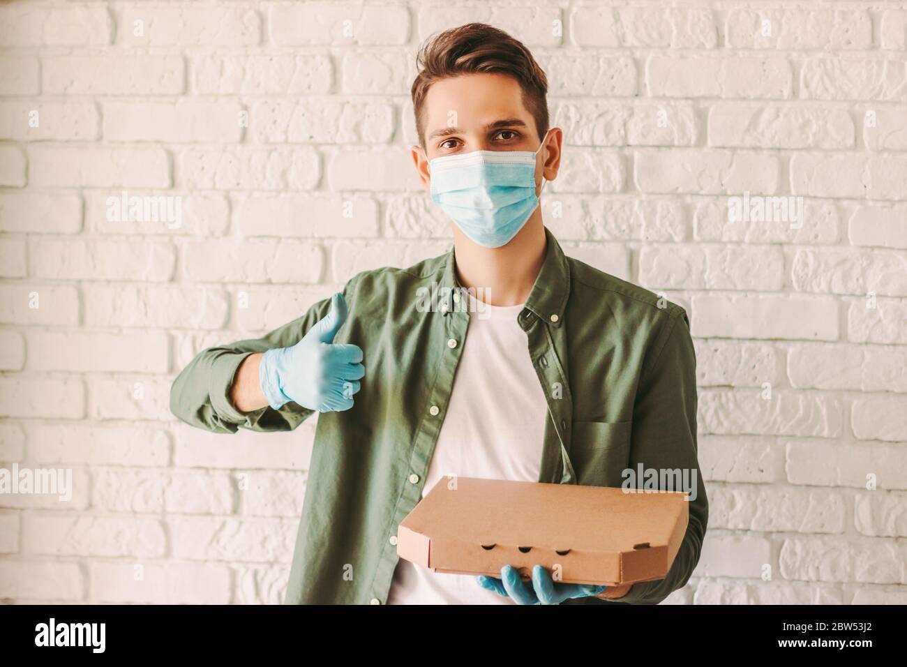 Happy delivery man in medical face mask and gloves hold cardboard pizza ...