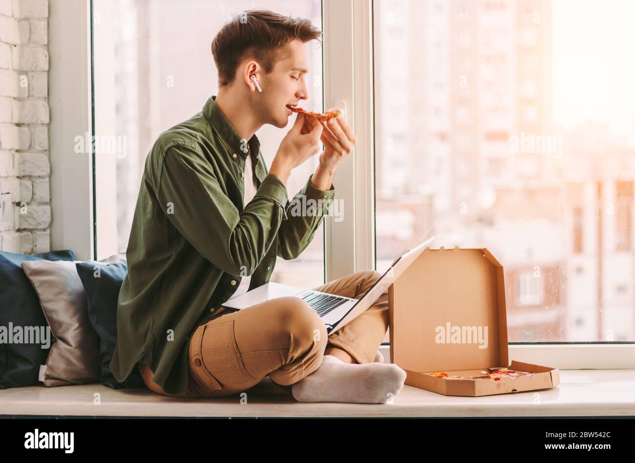Happy hipster man freelancer eat slice of tasty italian pizza, sit on ...