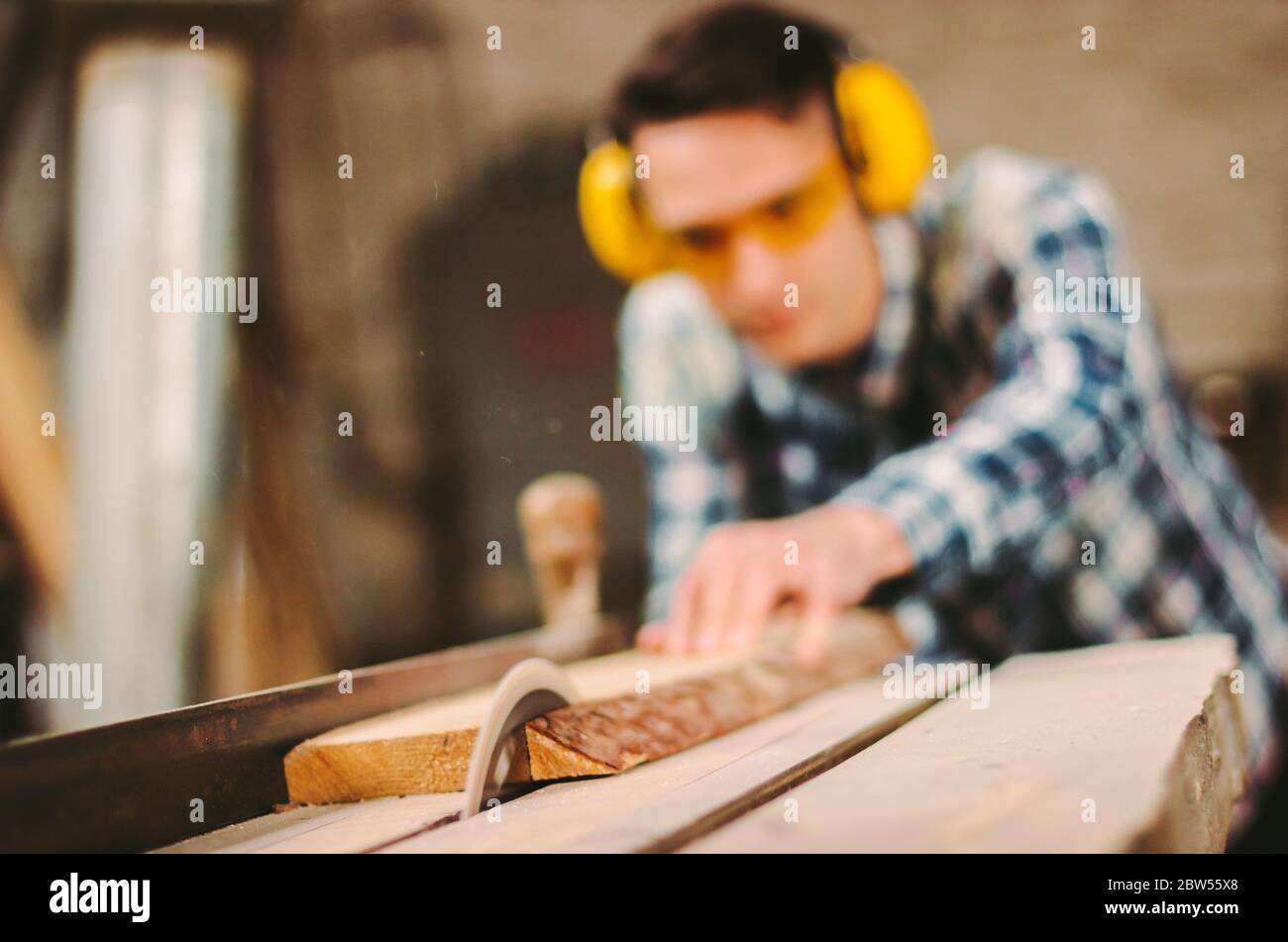 Professional carpenter using sawing machine for cutting wooden board at ...