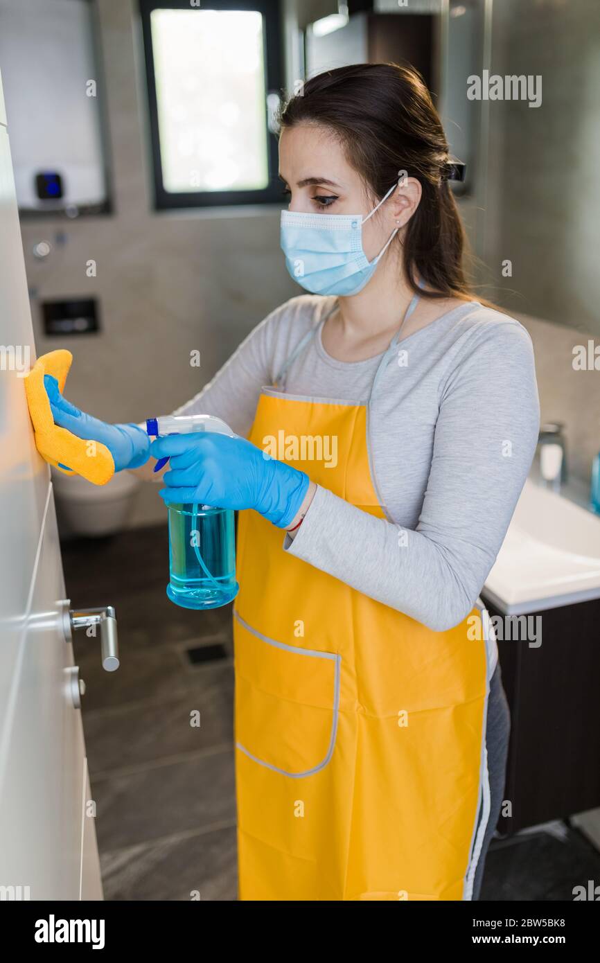 Woman housekeeper wipes the door with rag and using spray disinfectant ...