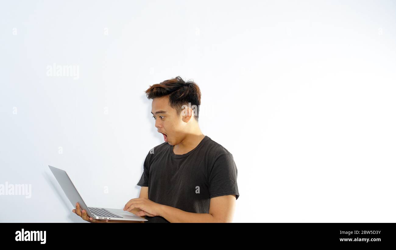 Surprised young Asian man with laptop isolated on white background ...