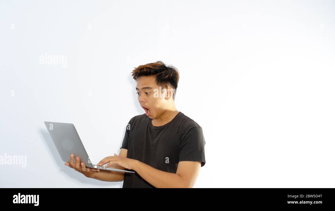 Surprised young Asian man with laptop isolated on white background ...