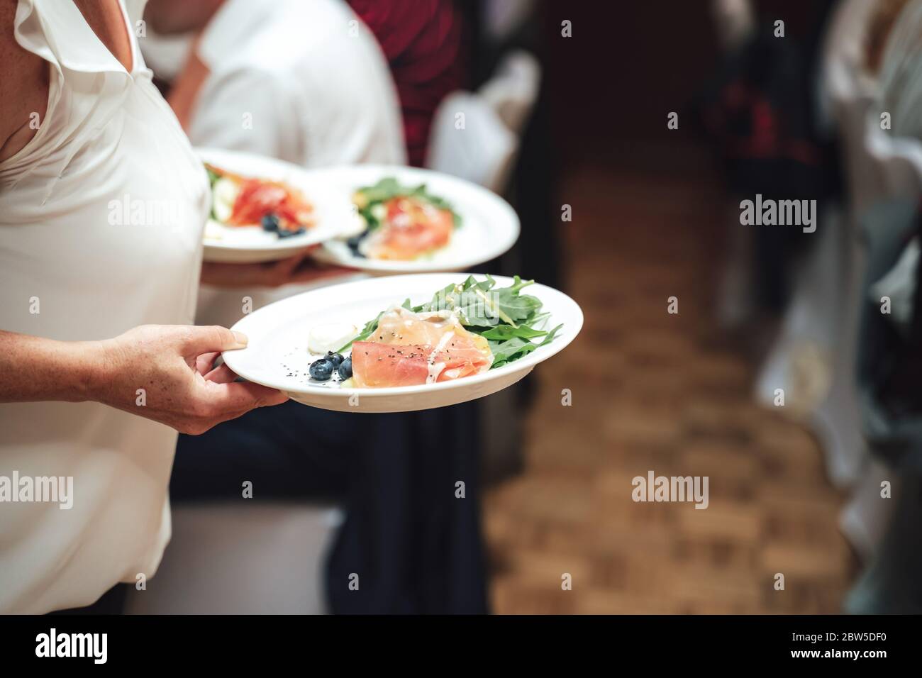 Woman carrying white plates with light snack. Slices of ham, garden ...