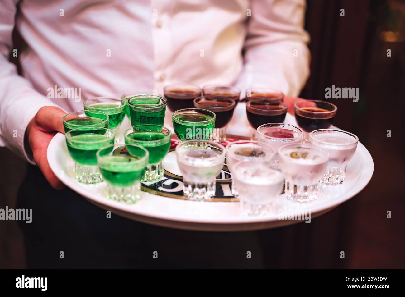 Man in shirt carrying tray with several various alcoholic drinks ...