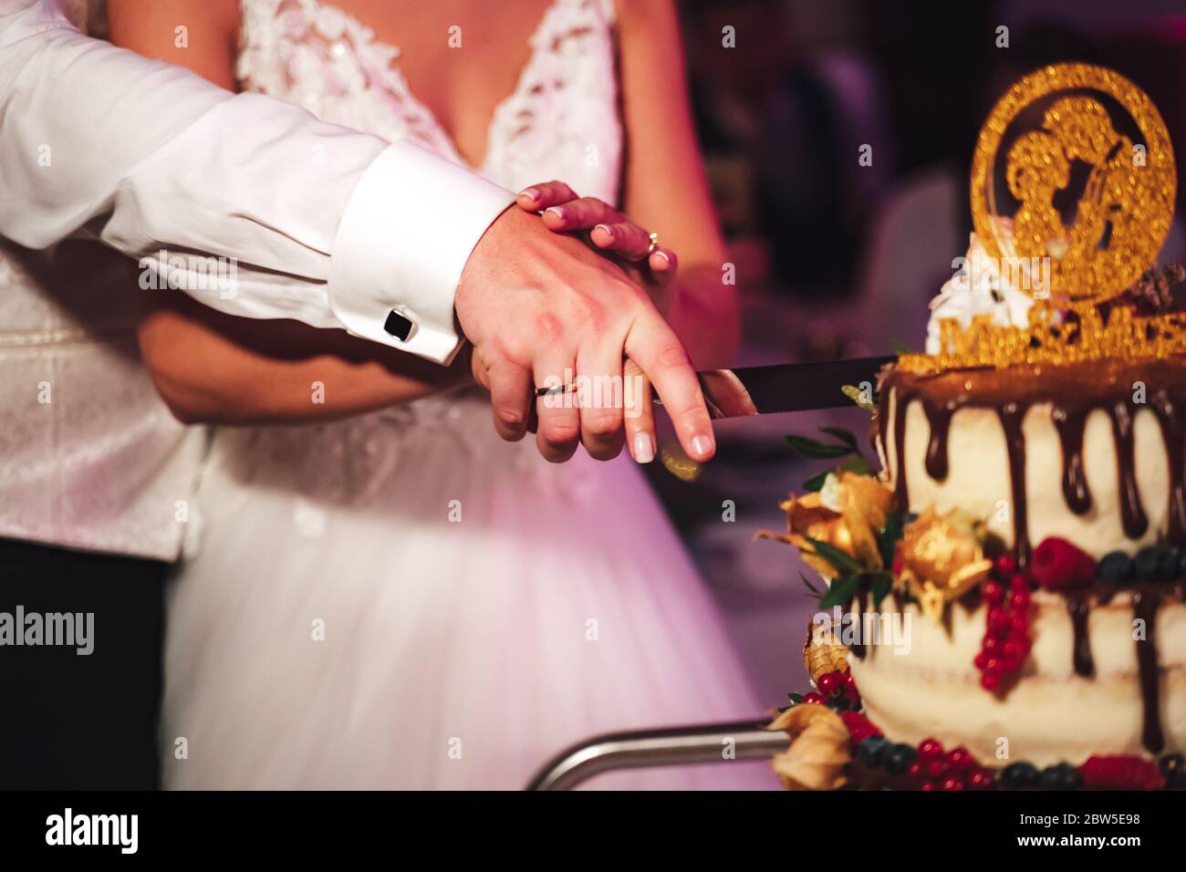 Wedding couple cutting wedding cake. Bride and groom holding knife in ...