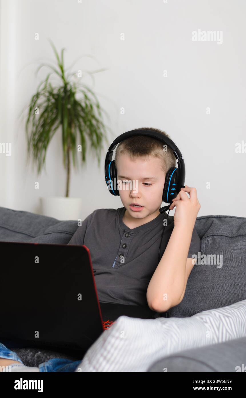 Boy talking on headphones and playing online video game on laptop ...