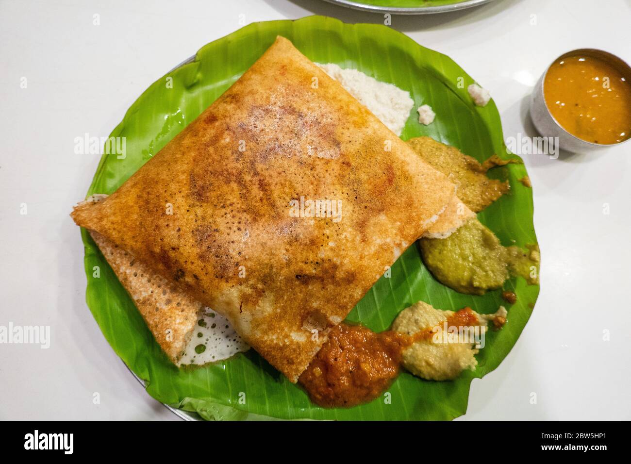 A thin folded dosa served on a leaf with chutney, sauces and sambar in ...