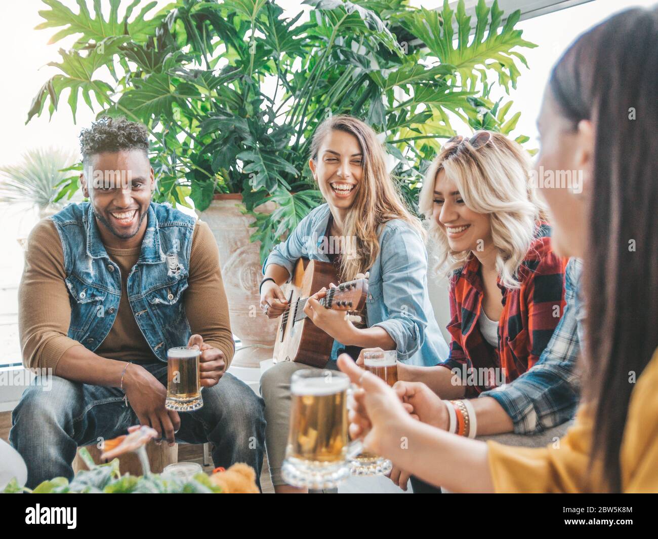 Young multicultural people having fun playing guitar and drinking beer ...