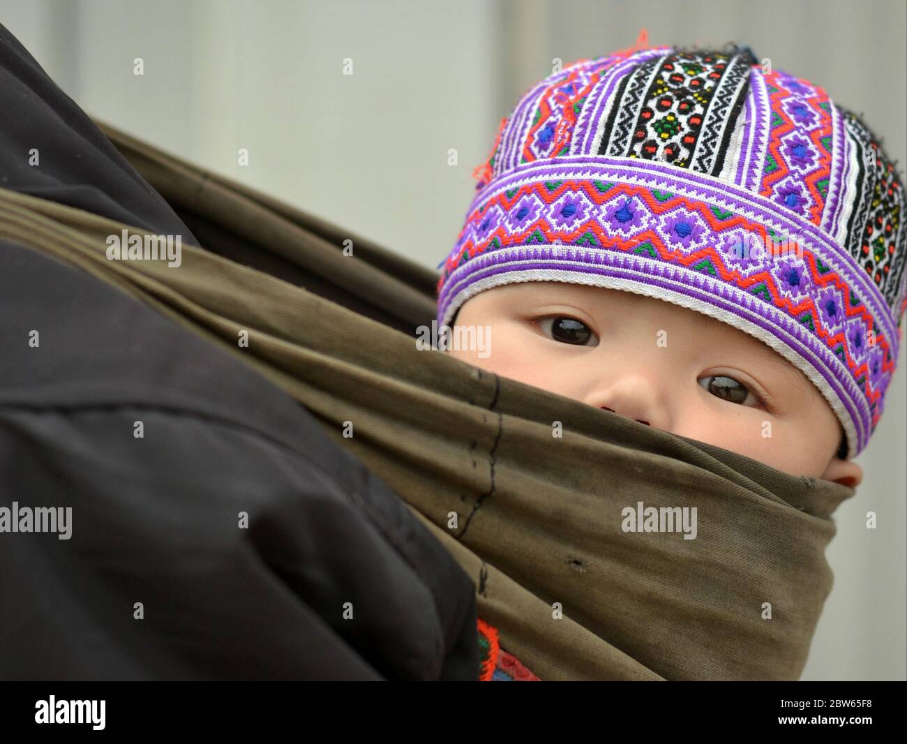 Cute Vietnamese H’mong baby boy sits in a baby sling and looks at the ...