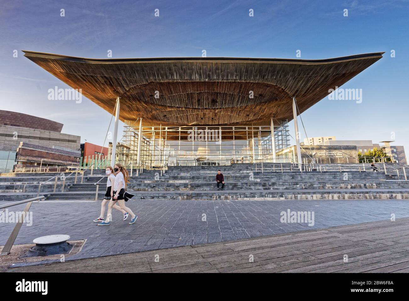 Two young people people who wear face masks walk past the Senedd, Welsh ...