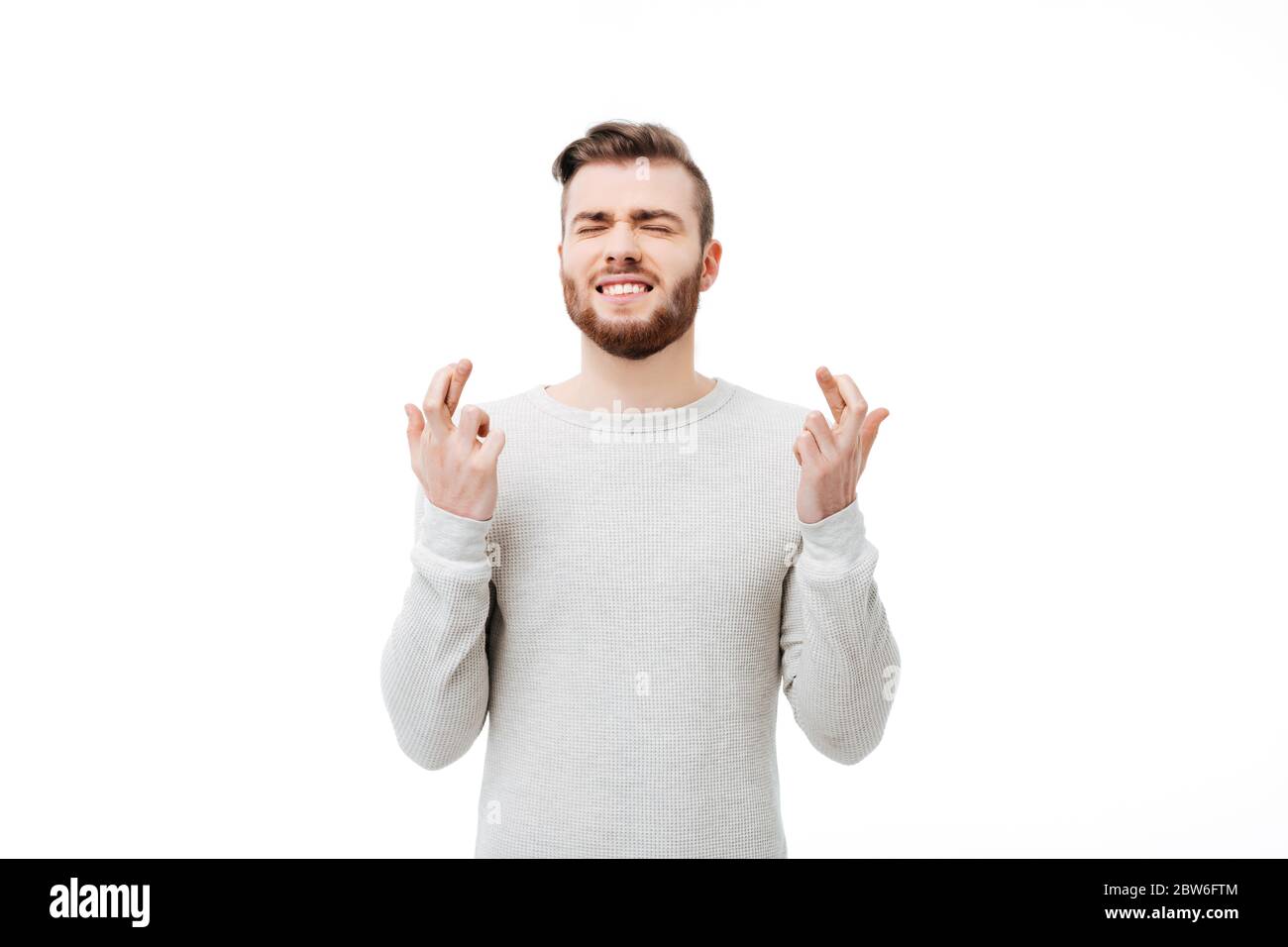 Young man making a wish emotionally with finger crossed gesture over ...