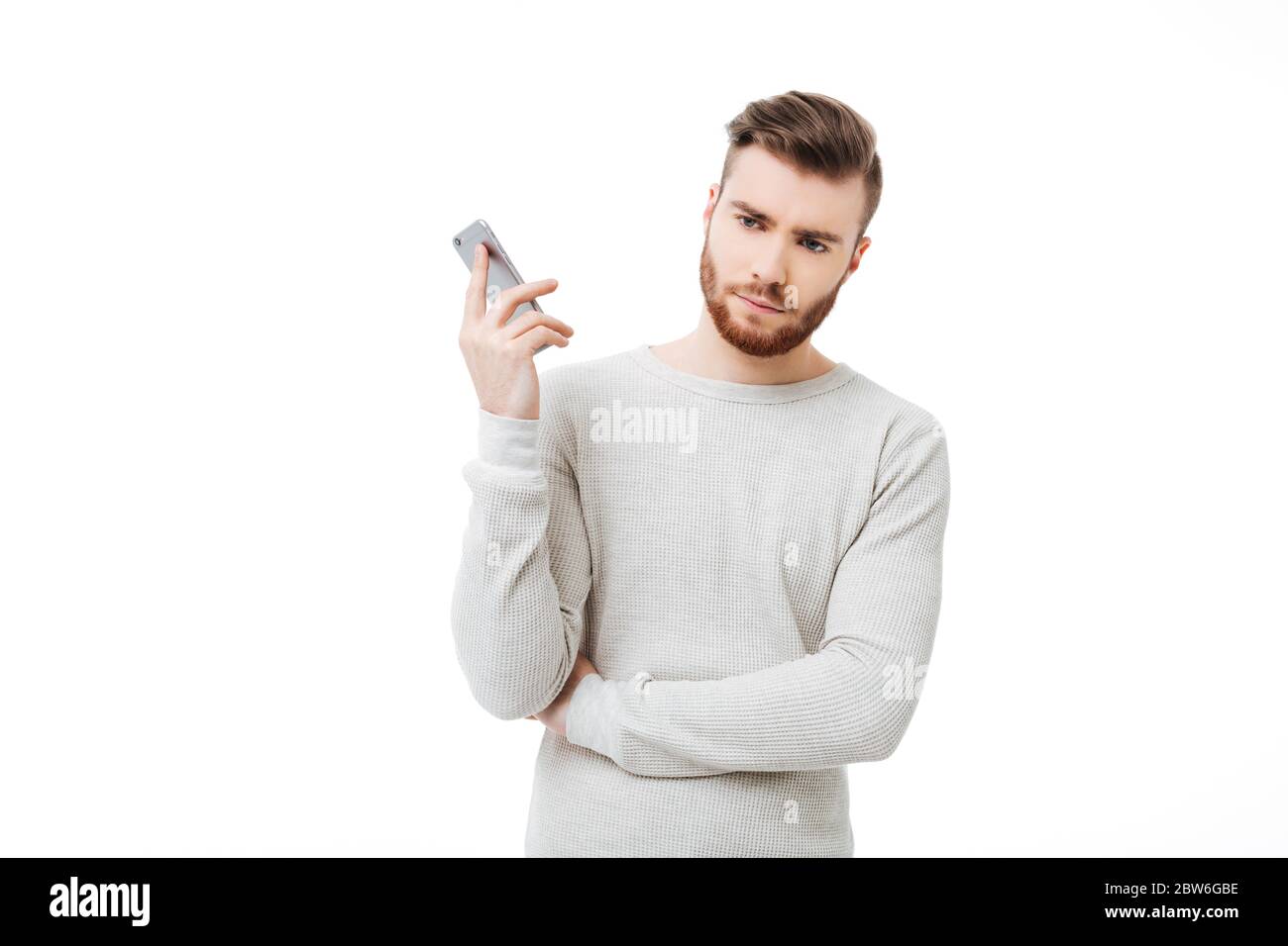 Annoyed young man holding smartphone far from his ear. Angry man doesn ...