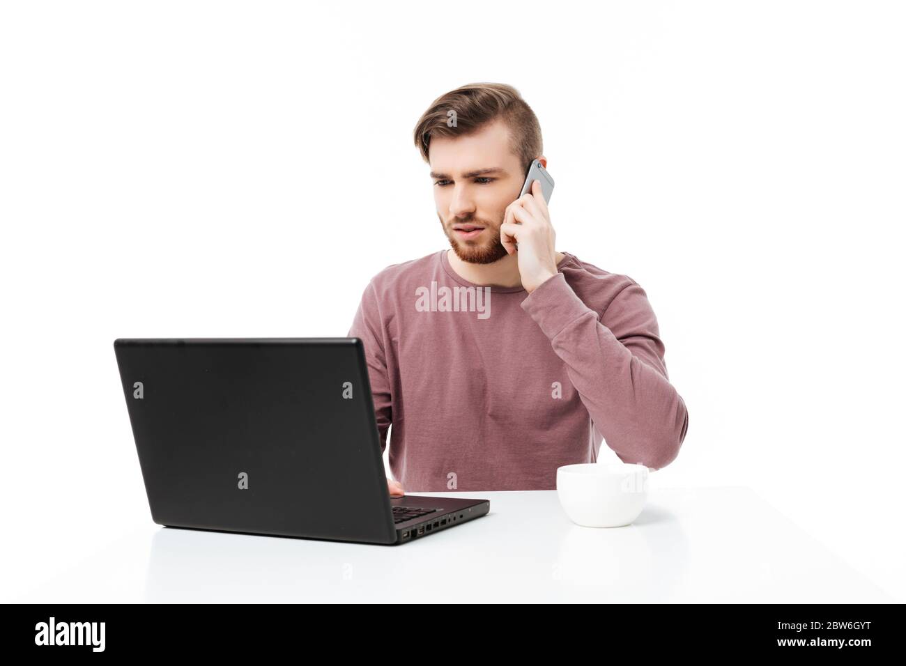 Upset young man working at the laptop computer talking on the phone ...