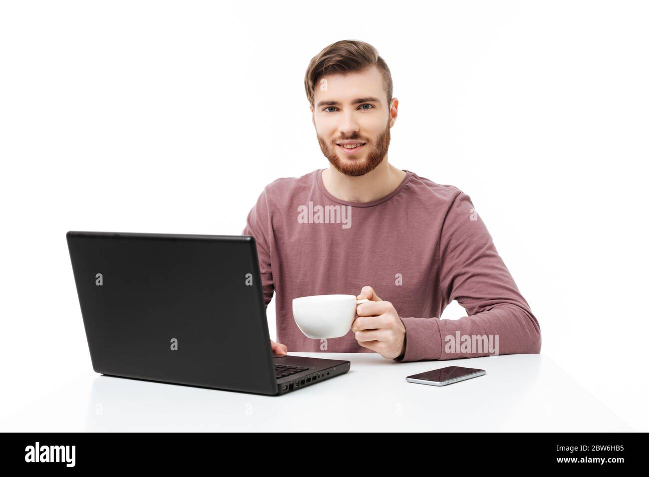 Attractive young man drinking coffee working at the laptop computer and ...