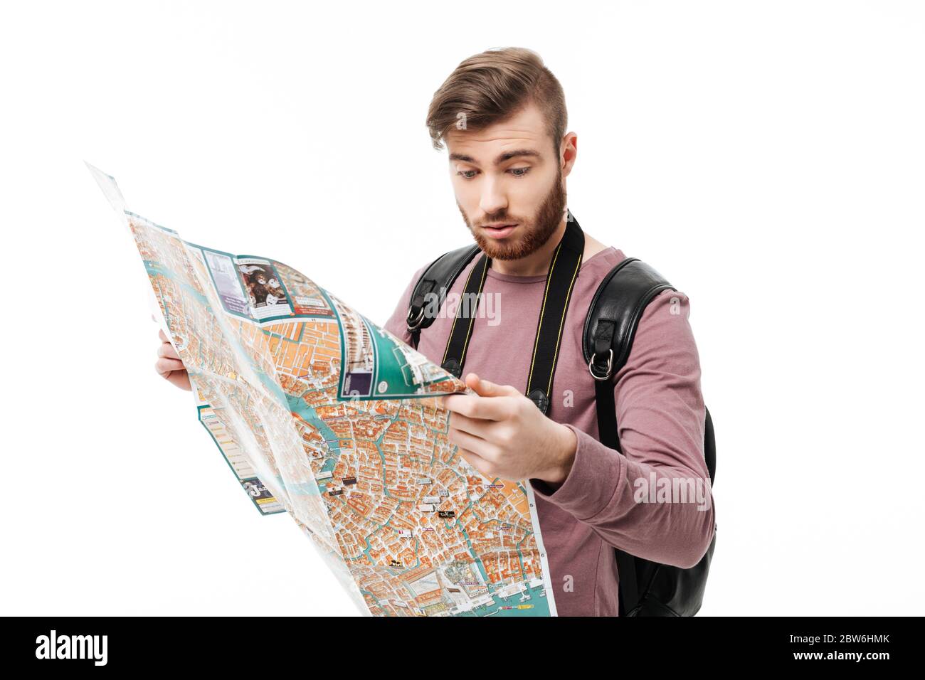 Young man amazedly looking in open map on white background. Portrait of ...