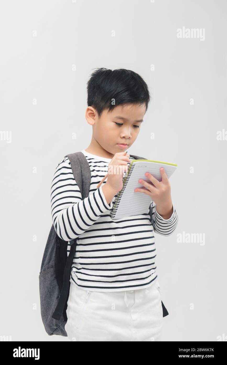 Young asian school boy writing in notepad with backpack on white ...