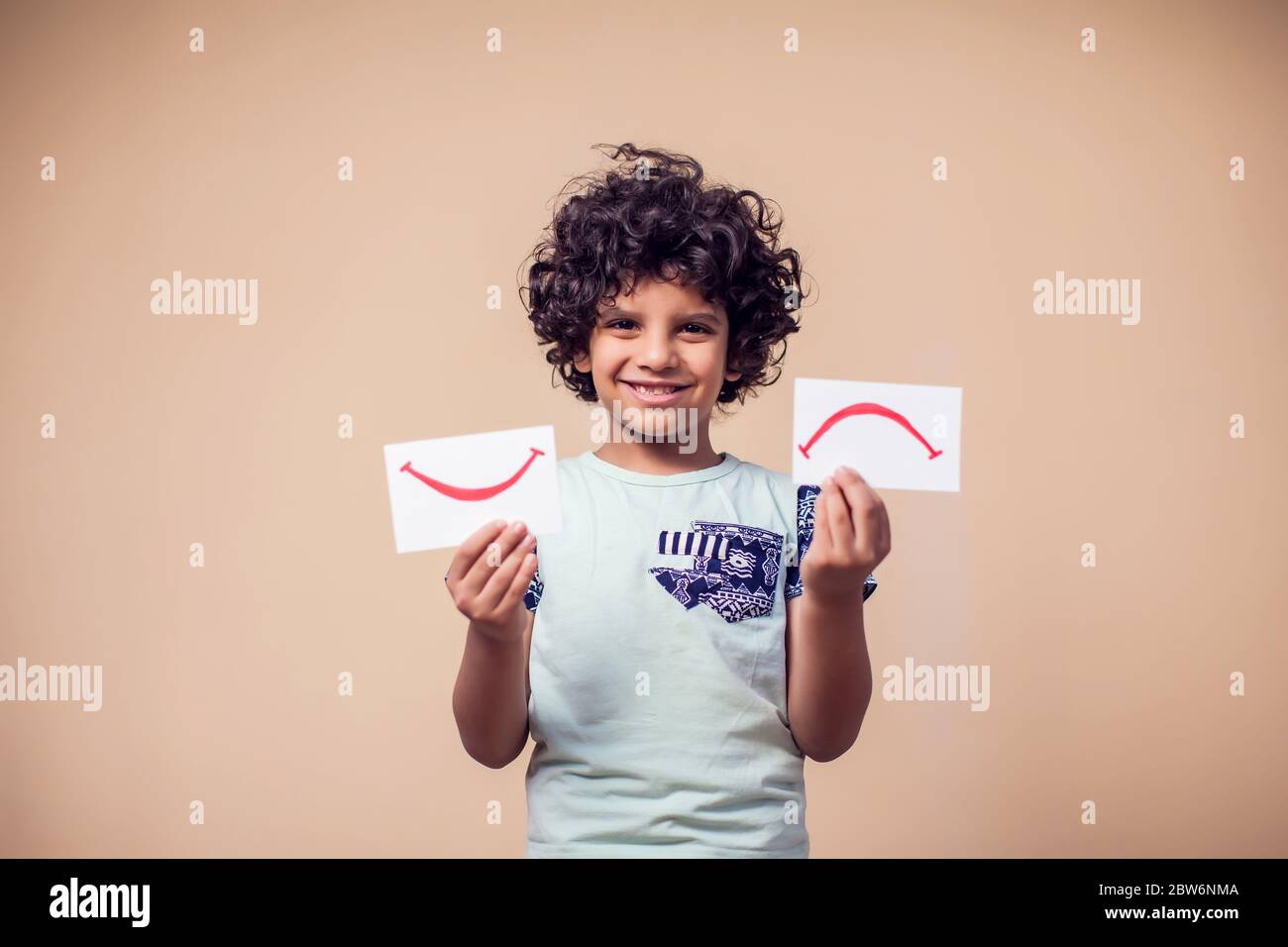 A portrait of kid boy holding cards with positive and negative symbol ...