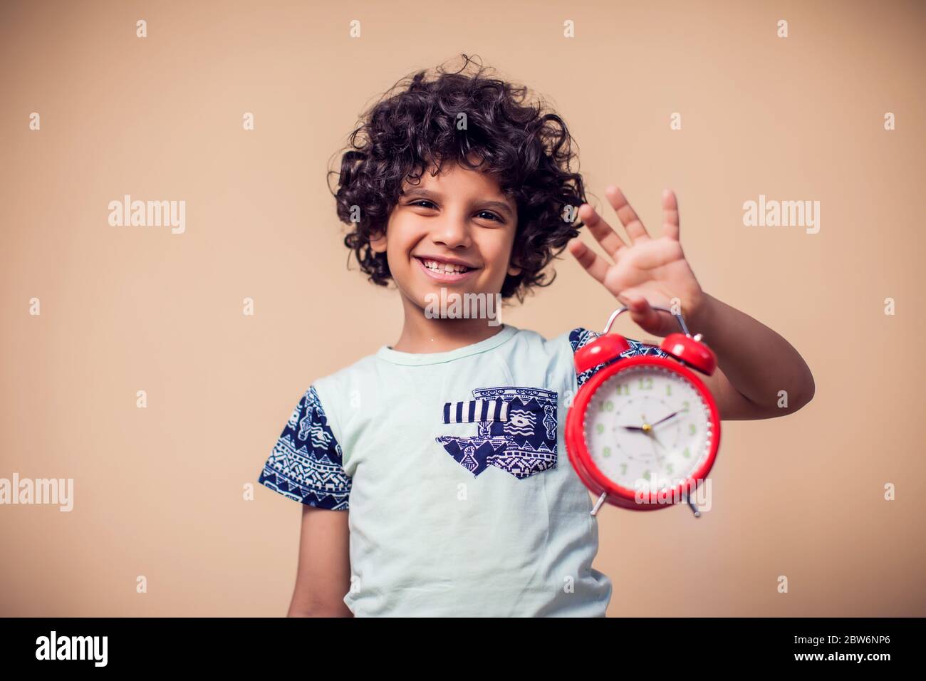 A portrait of kid boy holding red alarm clock. Children and time ...