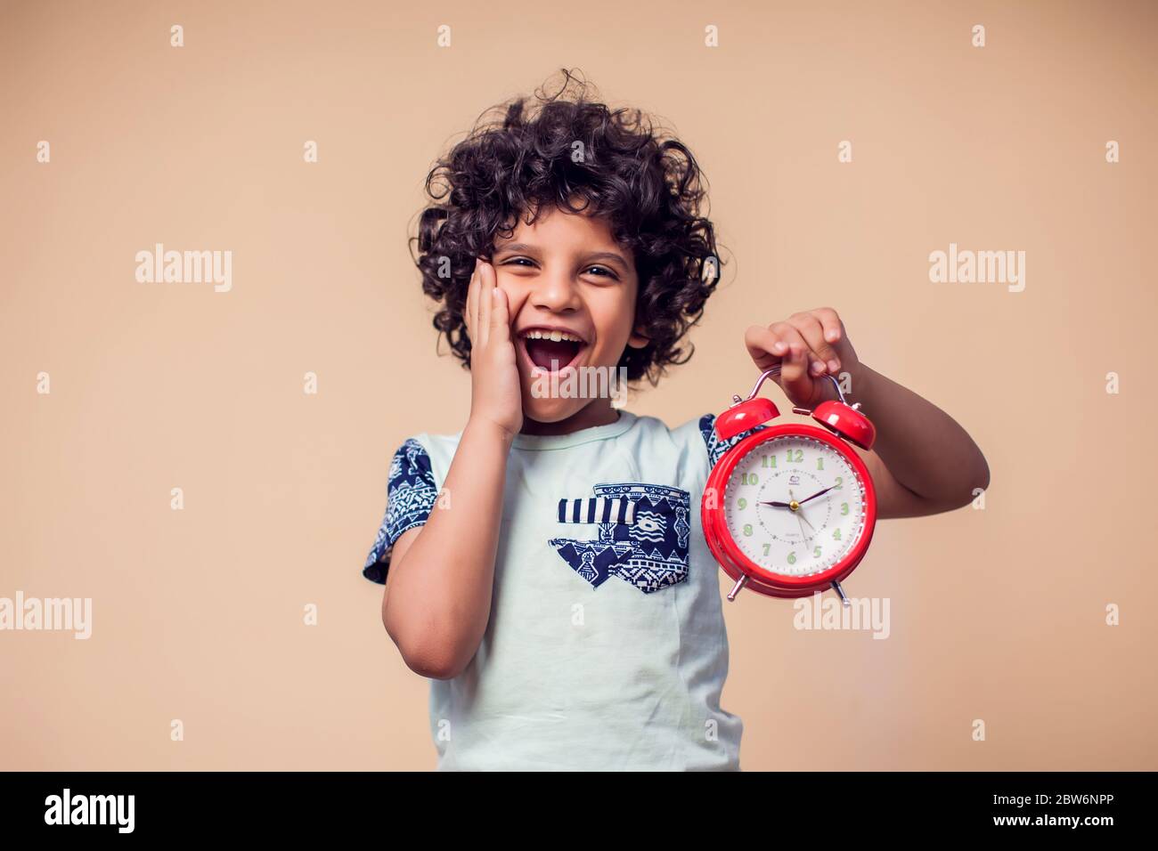 A portrait of surprised kid boy holding red alarm clock. Children and ...