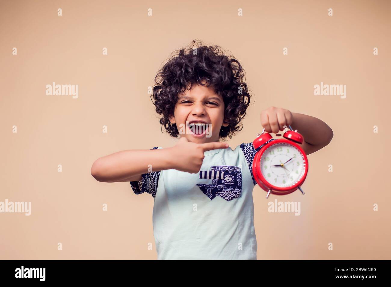 A portrait of surprised kid boy holding and pointing at red alarm clock ...