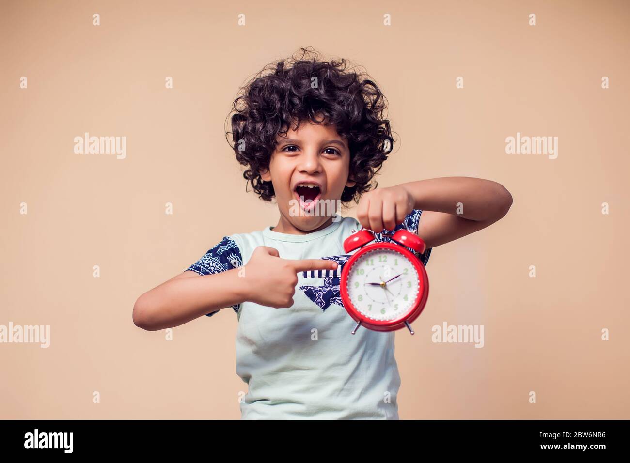 A portrait of surprised kid boy holding and pointing at red alarm clock ...