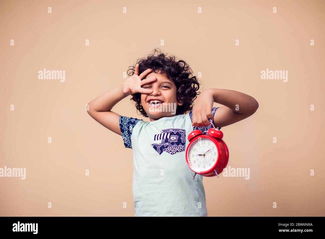 A portrait of yawning kid boy holding red alarm clock. Children and ...