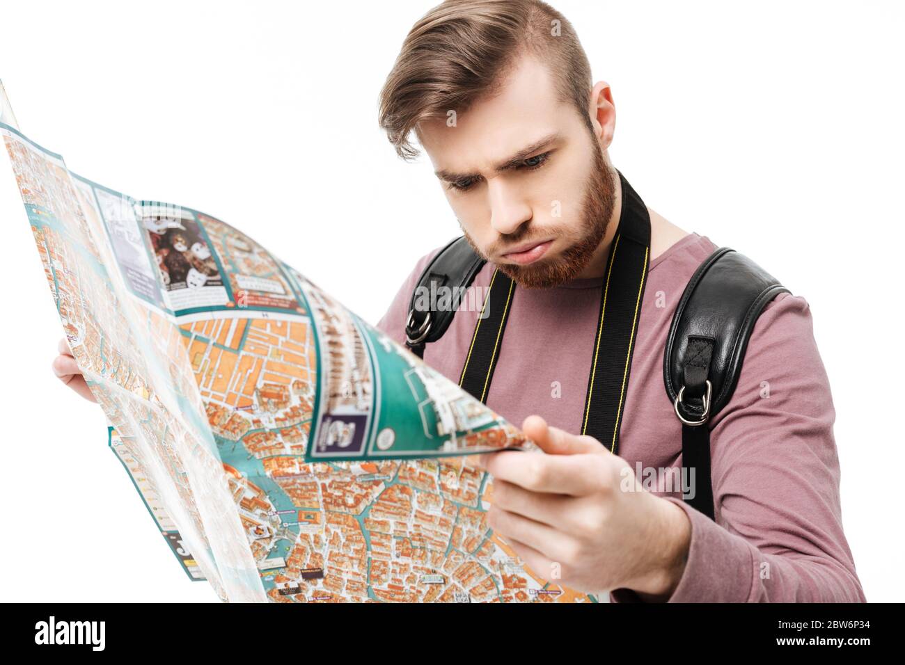 Young man thoughtfully looking in map in hands with backpack on white ...