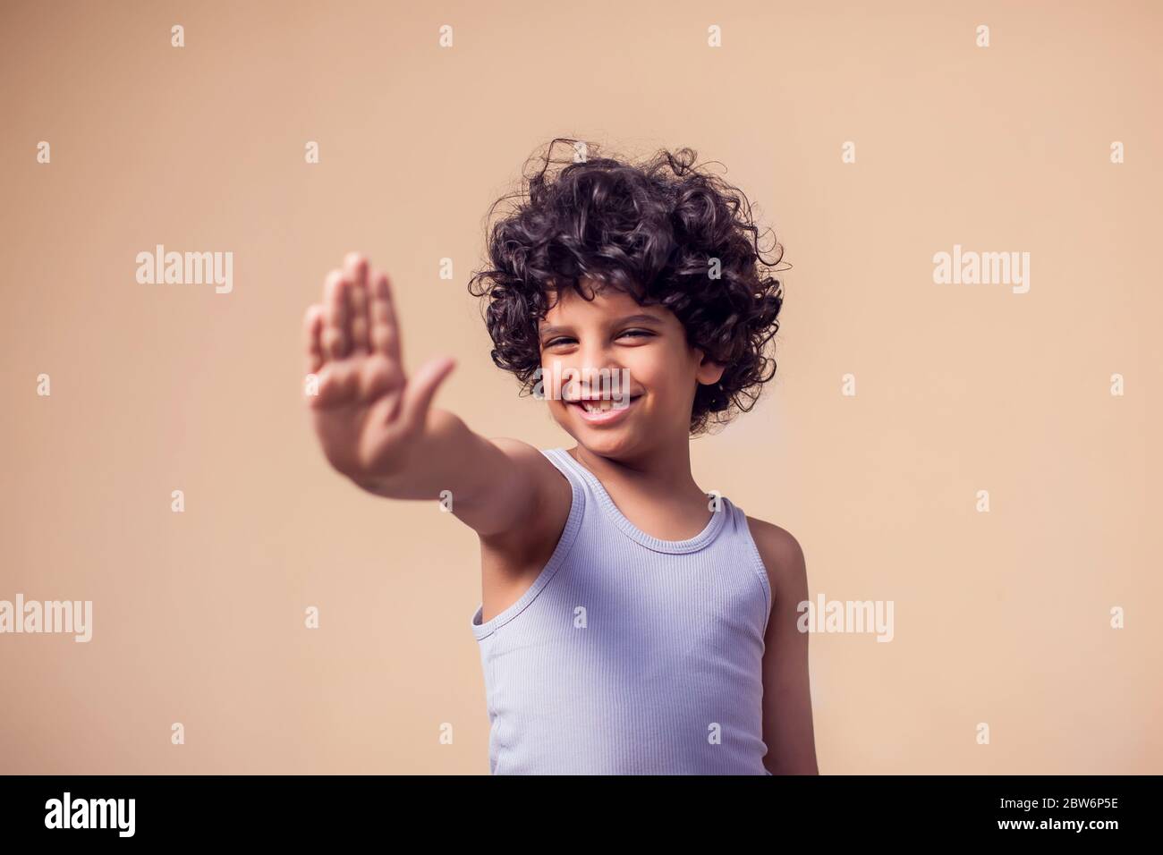 A portrait of angry kid boy with curly hair showing stop gesture ...