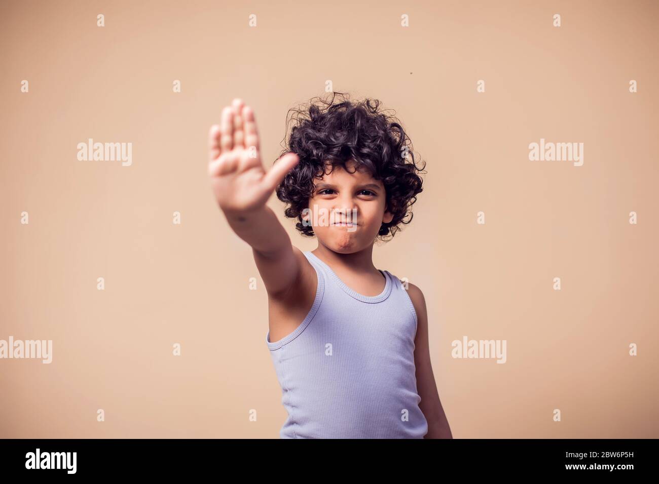 A portrait of angry kid boy with curly hair showing stop gesture ...