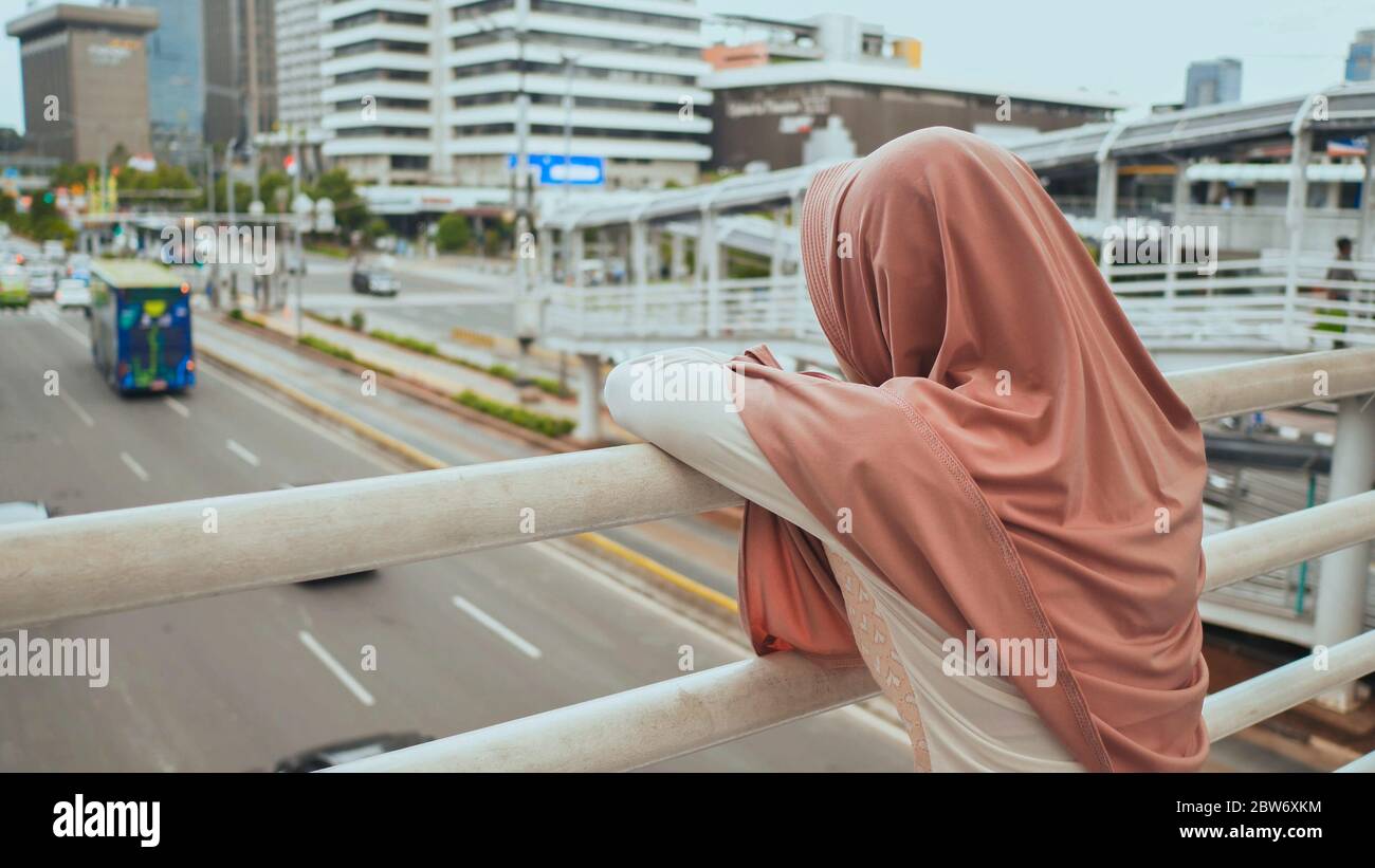 A young, sad Muslim girl stands on a bridge over road traffic in ...