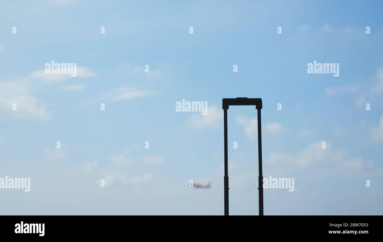 Handle from a suitcase against the blue sky with a plane taking off ...