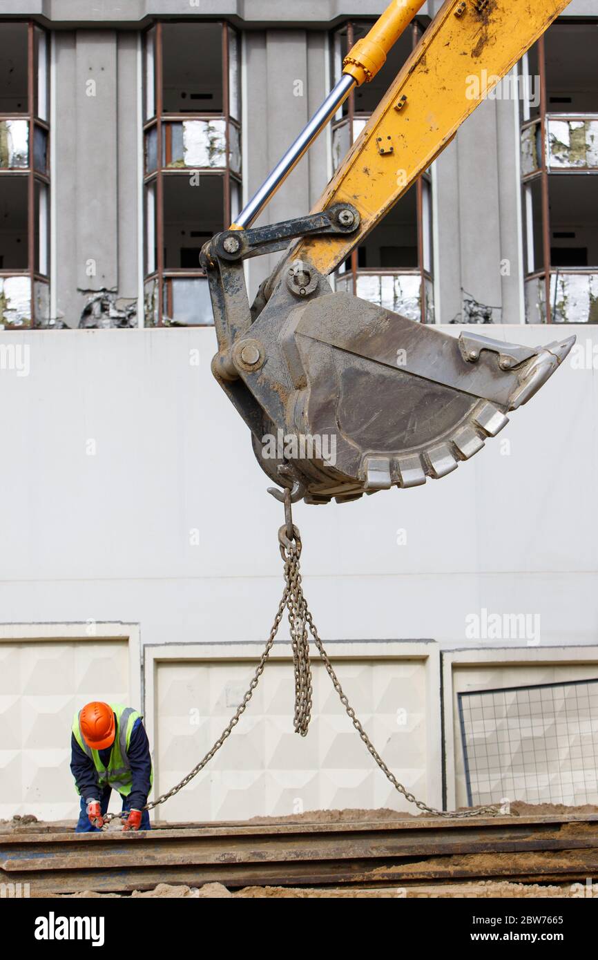 Excavator bucket lifting metal beam with worker helping, construction ...