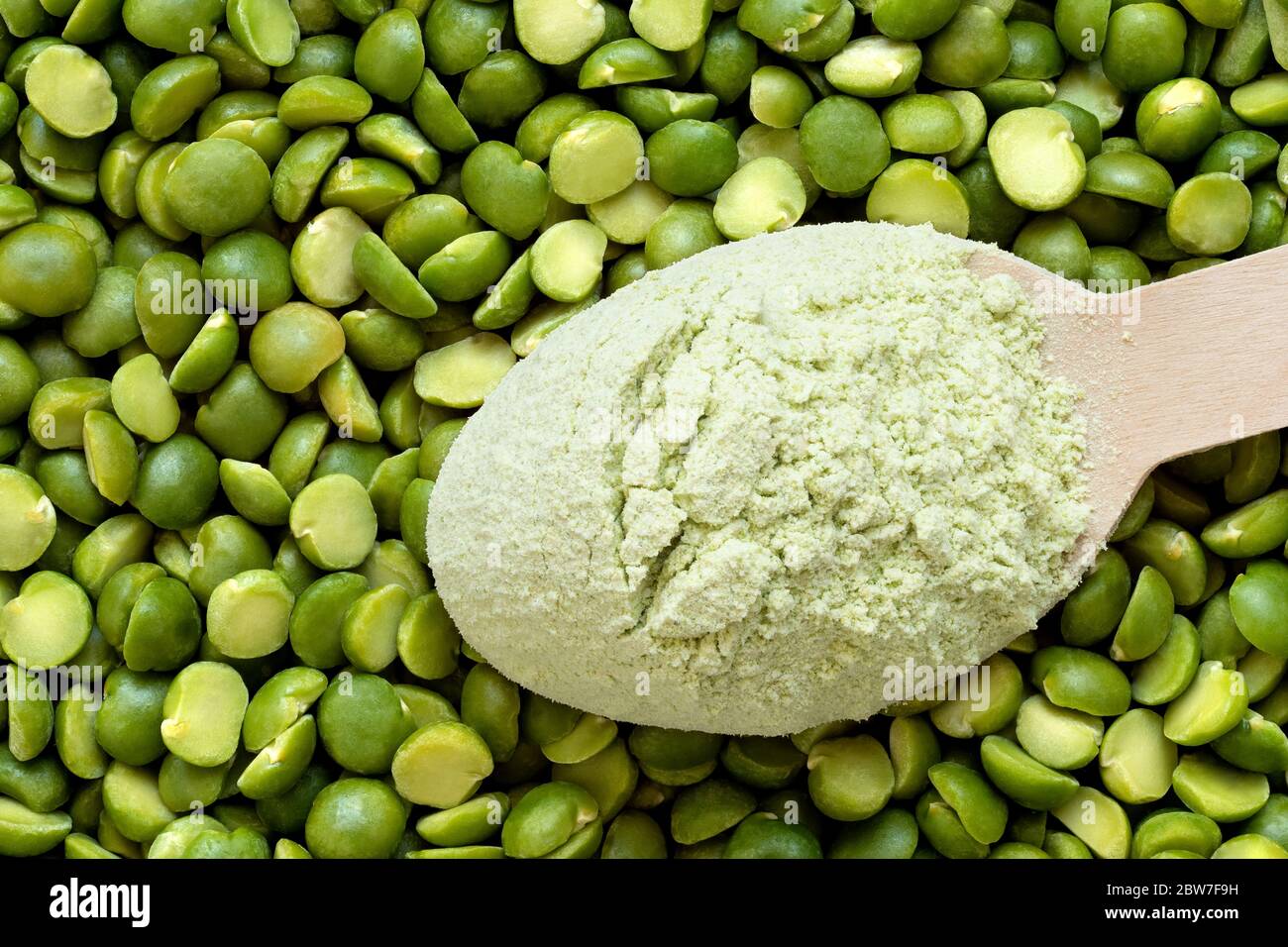 Wooden spoon of dried green pea flour on top of dried green split peas ...