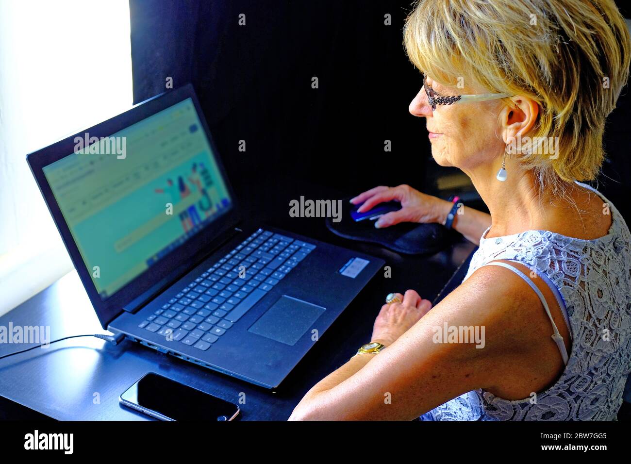 Lady in her 70's working on a computer with mobile phone handy Stock ...