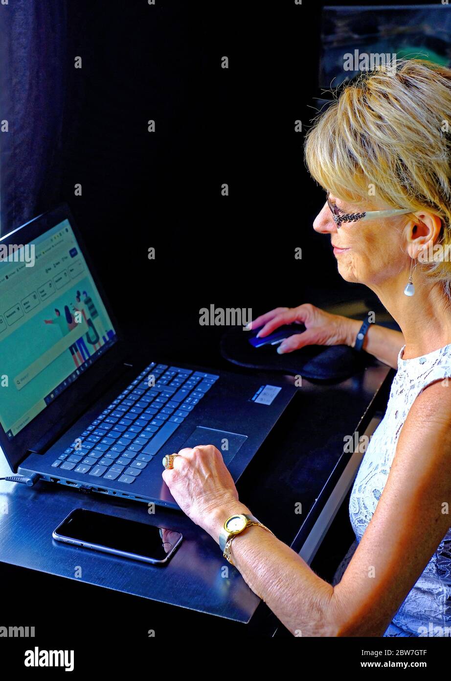 Lady in her 70's working on a computer with mobile phone handy Stock ...