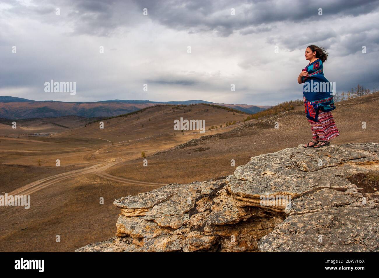 A girl stands on a stone block in the steppe. Model in a dress and ...