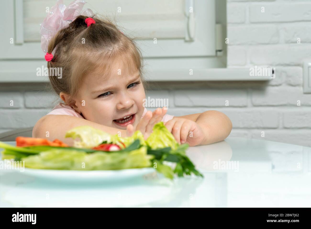 a little girl emotionally pushes away a plate of offered vegetables ...