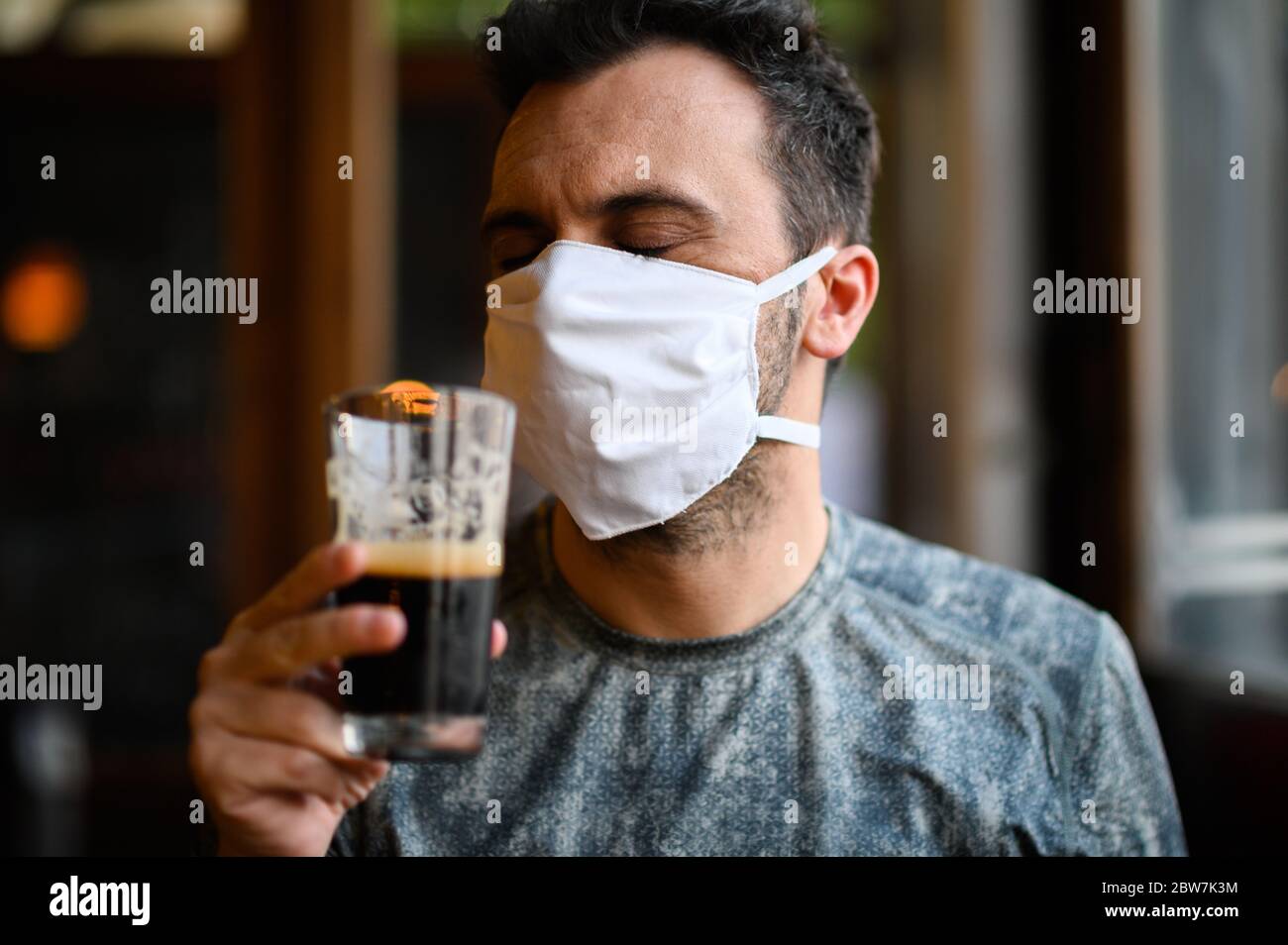 Young man trying to drink a beer wearing a mask, funny coronavirus ...