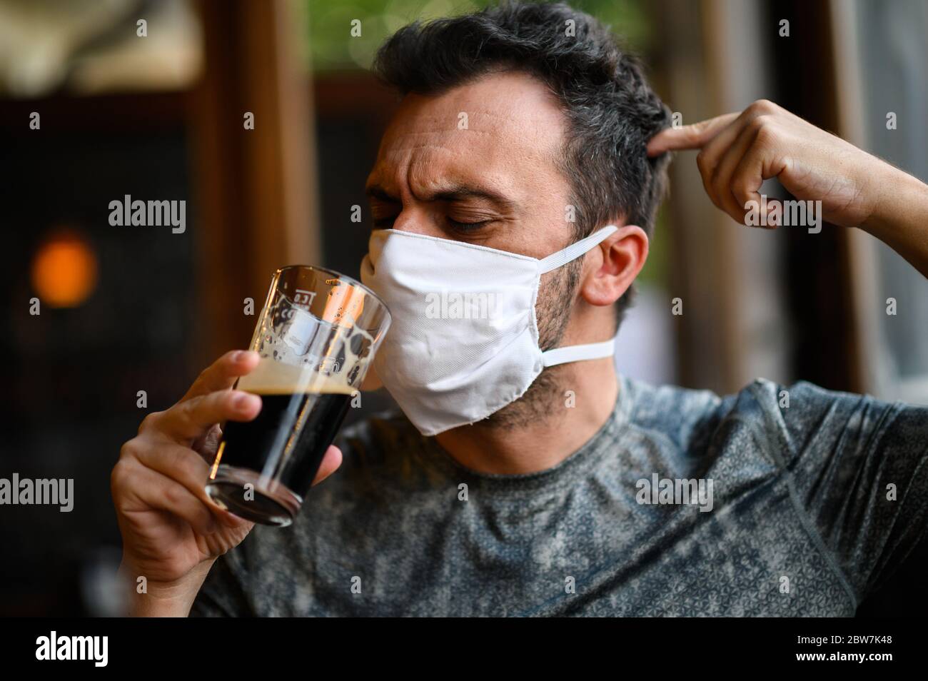 Young man trying to drink a beer wearing a mask, funny coronavirus ...