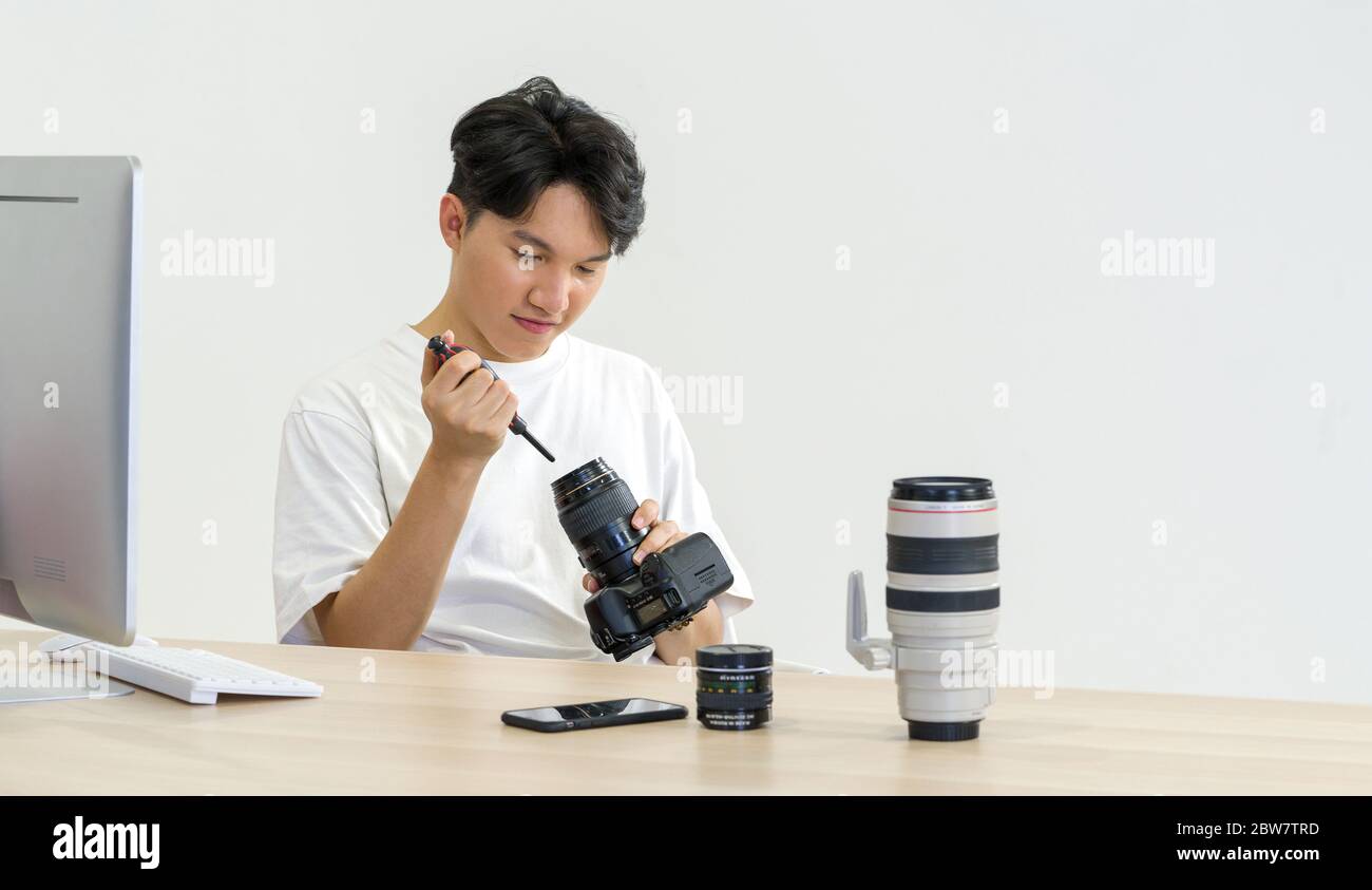 An Asian photographer is cleaning the camera and lens with a blower ...