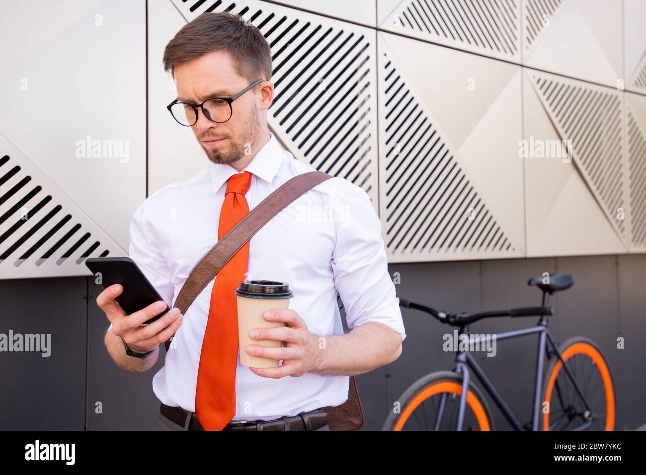 Serious man with glass of coffee and smartphone looking through ...
