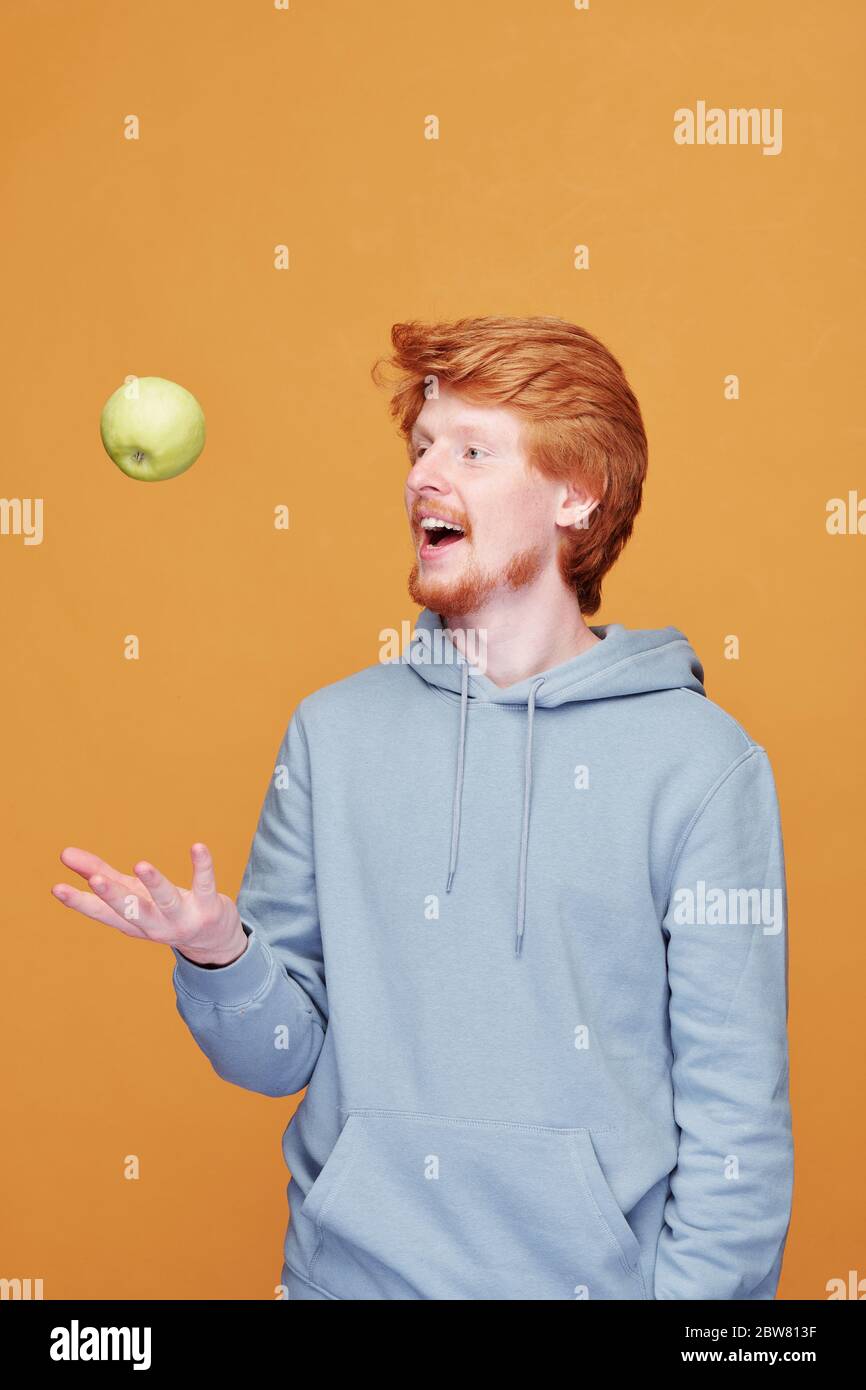 Happy young casual man throwing green apple in front of himself while ...