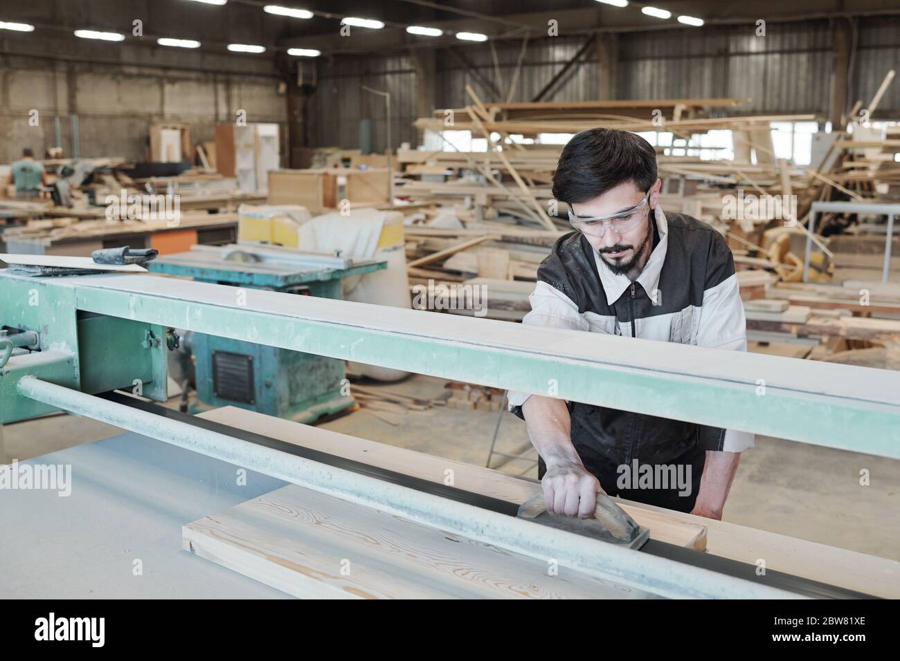 Young man in workwear bending over workbench and smoothing surface of ...