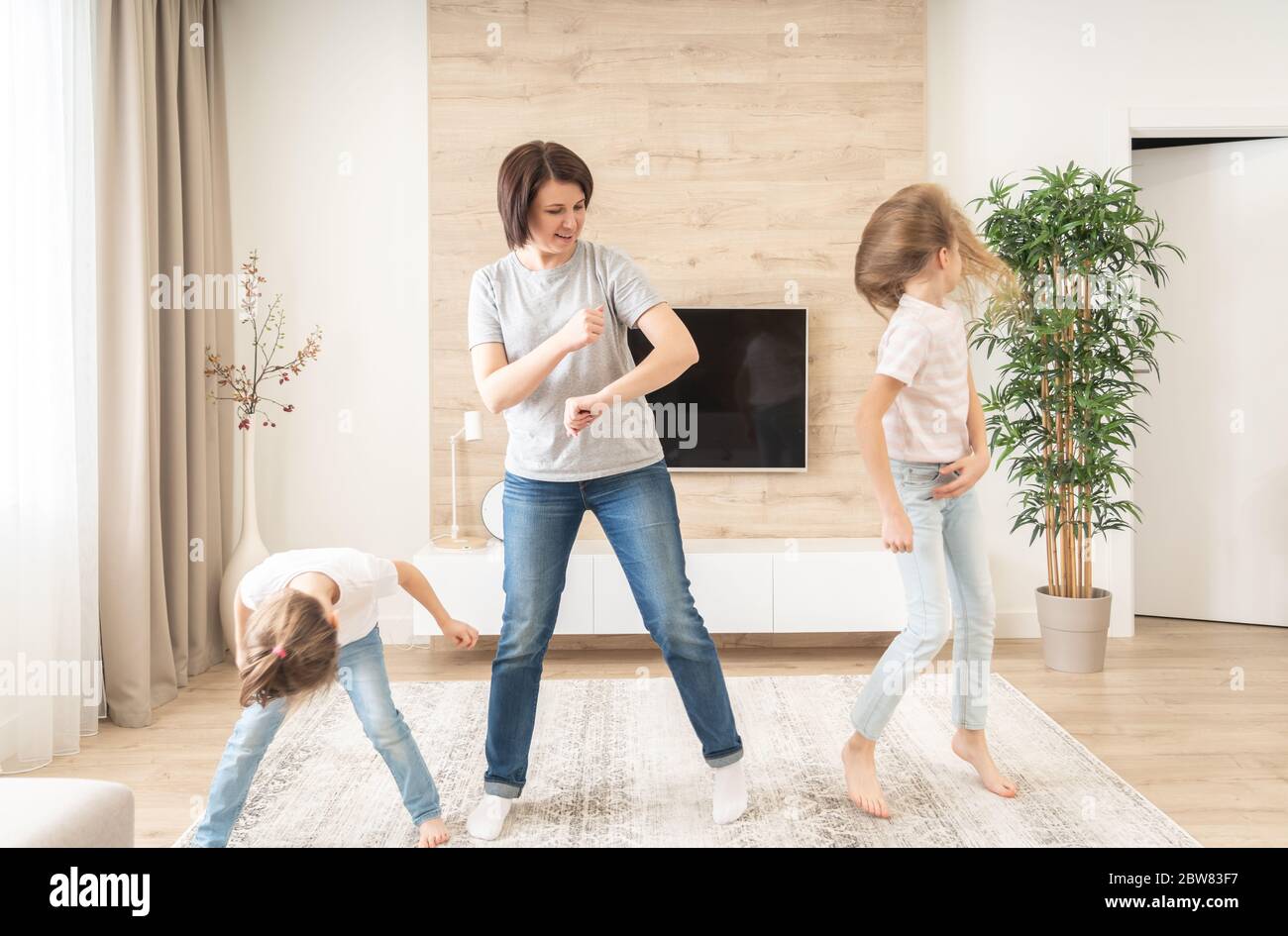 Happy mother and two daughters having fun dancing in living room. mother laughing enjoying funny ...