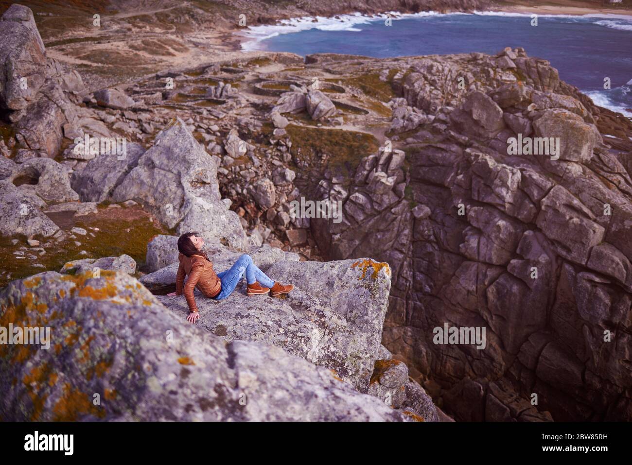 young woman sitting on a cliff near the Baroña celtic castro Stock ...