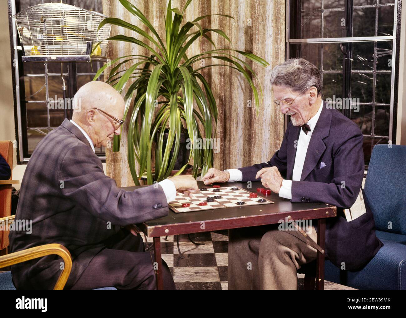 1960s TWO ELDERLY MEN PLAYING A GAME OF CHECKERS IN LOUNGE WITH HOUSE ...