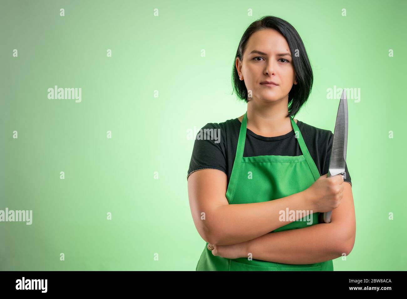 Female cook with green apron and black t-shirt, looking confident with ...